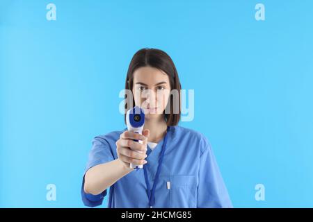 Female nurse with thermometer gun on blue background Stock Photo - Alamy