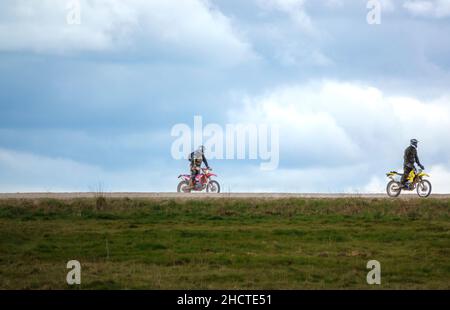 a pair of motorcyclists riding motorbikes across an unmade stone track ...