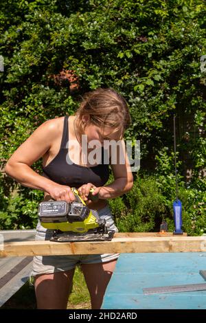 Young woman using electric power sawing tool without safety googles or ...