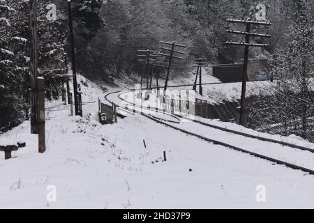 Railroad tracks next to a hill covered with snow and aerial wires in ...