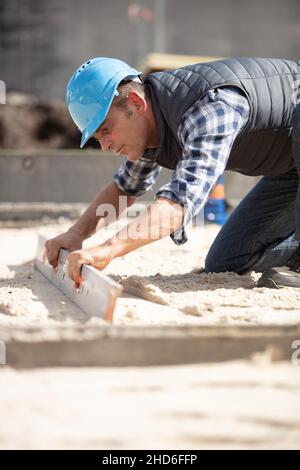 Low angle view of a man leveling fresh cement to build a foundation in ...