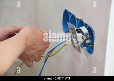 Electrician worker is attaching wires to new electrical outlet ...