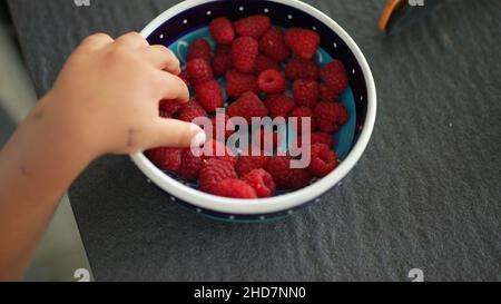 Hand grabbing raspberry fruit from bowl Stock Photo - Alamy