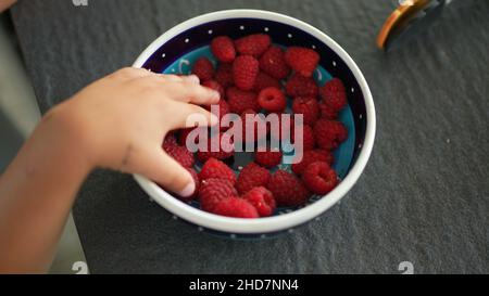 Hand grabbing raspberry fruit from bowl Stock Photo - Alamy