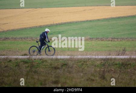 a casual peddle bike cyclist riding along an unmade track crossing open ...