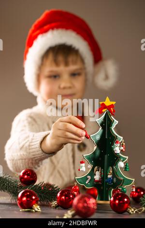 Boy in santa hat decorates wooden vintage christmas tree with toys ...