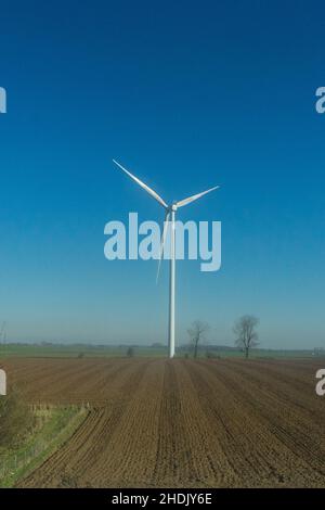 A vertical shot of tall wind turbine in the field on blue sky ...