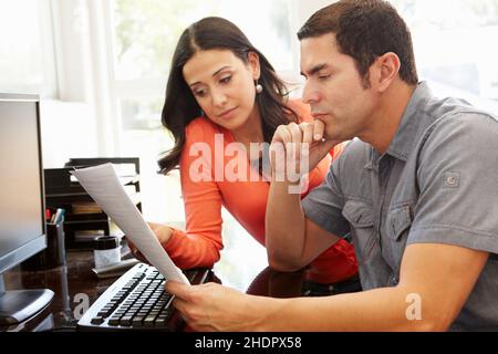 Serious couple sitting at desk with documents and counting budget Stock ...