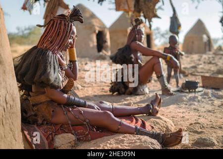 Himba women sitting outside their huts in a traditional Himba village ...