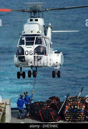 Sailors hook cargo to an AS 332 helicopter, preparing for aerial ...