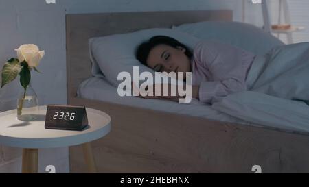 Clock and flower on bedside table near blurred man on bed at home Stock ...