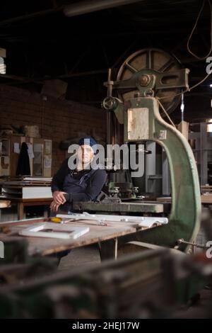 Young male craftsperson holding wooden plank on workbench while working ...