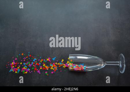 A wine glass with splashes of confetti on dark background. Copy space ...