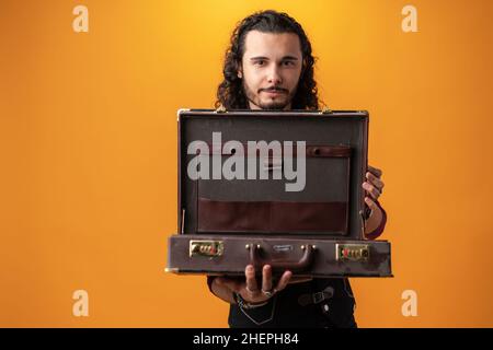 Young man with cirly long hair showing a briefcase against yellow ...