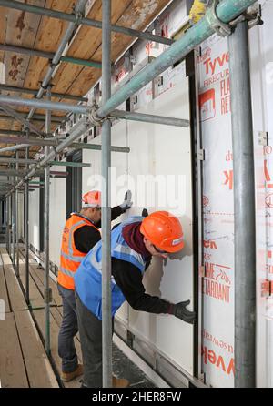 Workmen fix fire-resistant cladding panels and extra thermal insulation ...