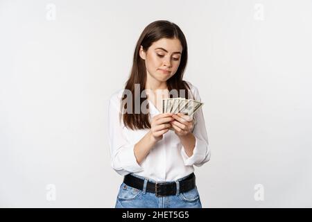 Sad woman counting money, lacking cash, standing gloomy over white ...