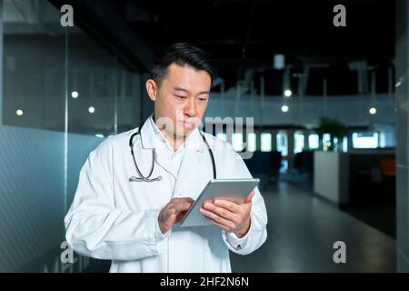 Serious Asian doctor, uses a tablet computer, the man works in a modern ...