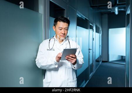 Serious Asian doctor, uses a tablet computer, the man works in a modern ...