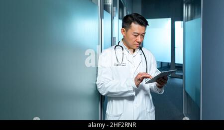 Serious Asian doctor, uses a tablet computer, the man works in a modern ...