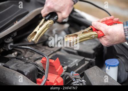 Hands of car mechanic using cables to start a car engine; panoramic ...