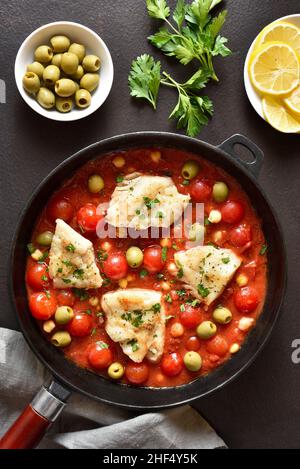 Cod stew with chickpeas, cherry tomatoes and olives over dark stone ...