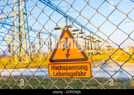warning sign at hight voltage tower in rural landscape with blue sky ...
