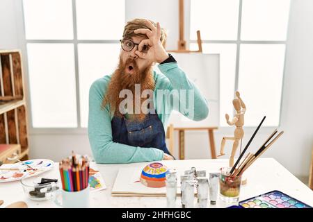 Redhead man with long beard painting clay bowl at art studio very happy ...