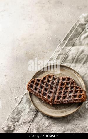 Two homemade waffles in the form of hearts lie side by side on a dark ...
