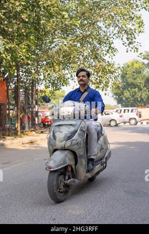 Common man riding a scooty on city street Stock Photo - Alamy