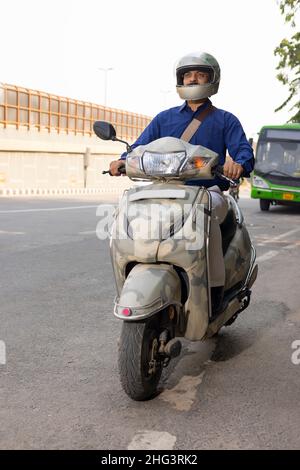 Common man riding a scooty on city street Stock Photo - Alamy