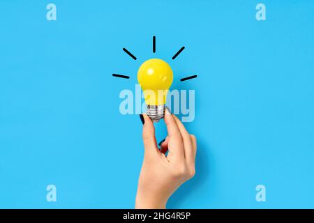 Female hand hold yellow light bulb on blue background Stock Photo - Alamy