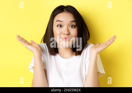 Silly mistake. Close up of cute asian girl saying sorry, shrugging ...