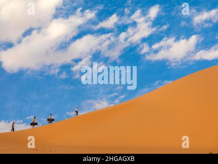 Group of friends climbing a dune to sandboard in Rub al Khali desert ...