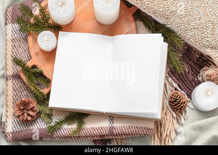 Opened book with blank pages, burning candles and winter decor on ...