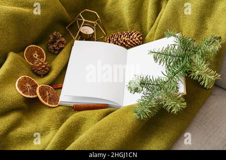 Opened book with blank pages, dried orange and fir tree branch on plaid ...