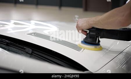 Auto mechanic grinds white car part after painting before polishing ...