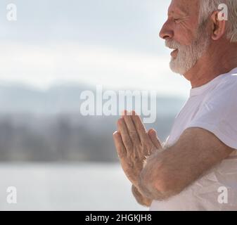 Portrait of senior man holding namaste pose and meditating outdoor ...