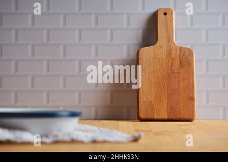 Wooden chopping board placed near wall on table with bowl in light ...