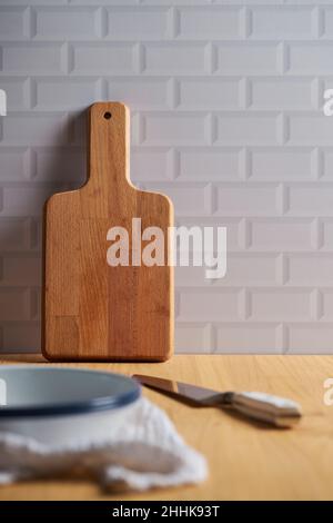 Wooden chopping board placed near wall on table with bowl in light ...