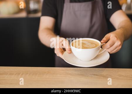 Crop male barista in apron serving cup of coffee while working at bar ...