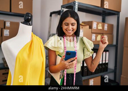 Young latin woman dressmaker with winner expression using smartphone at ...