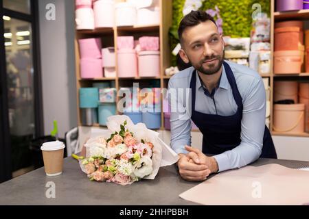 tired florist smiling looking at camera next to bouquet of flowers ...