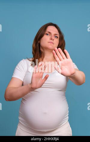 Portrait of a pregnant woman with a stop gesture on a white background ...