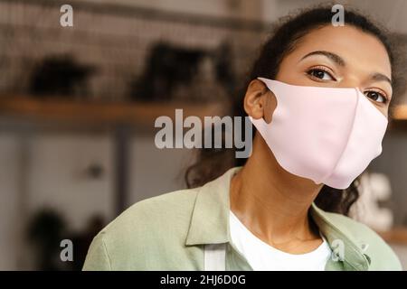 Black waitress wearing face mask holding paper bag while standing in ...
