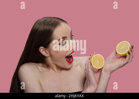 Excited beauty model with cut lemon in hands looking sideways isolated ...