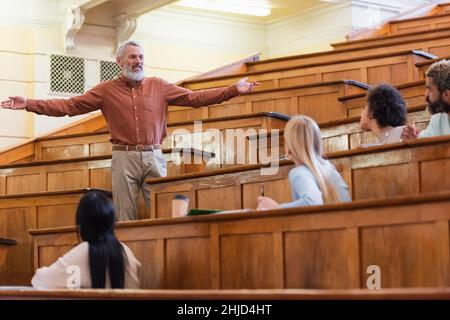 Mature professor holding chalk near multiethnic students in university ...