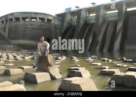 A man sits on concrete blocks under a dam. Dam and Waterfall Bendungan ...