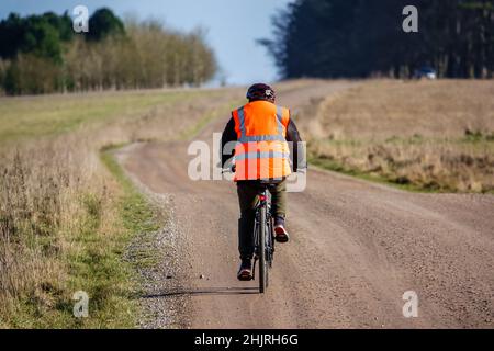 a casual cyclist in an orange high-vis jacket riding on a stone track ...