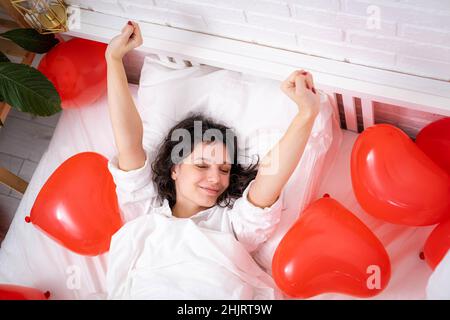 Brunette European girl sleeping on bed with red heart shape balloons ...