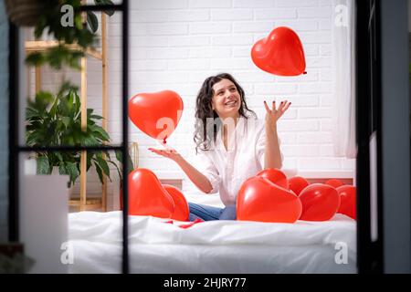 Brunette European girl rejoices playing on bed with red heart shape ...